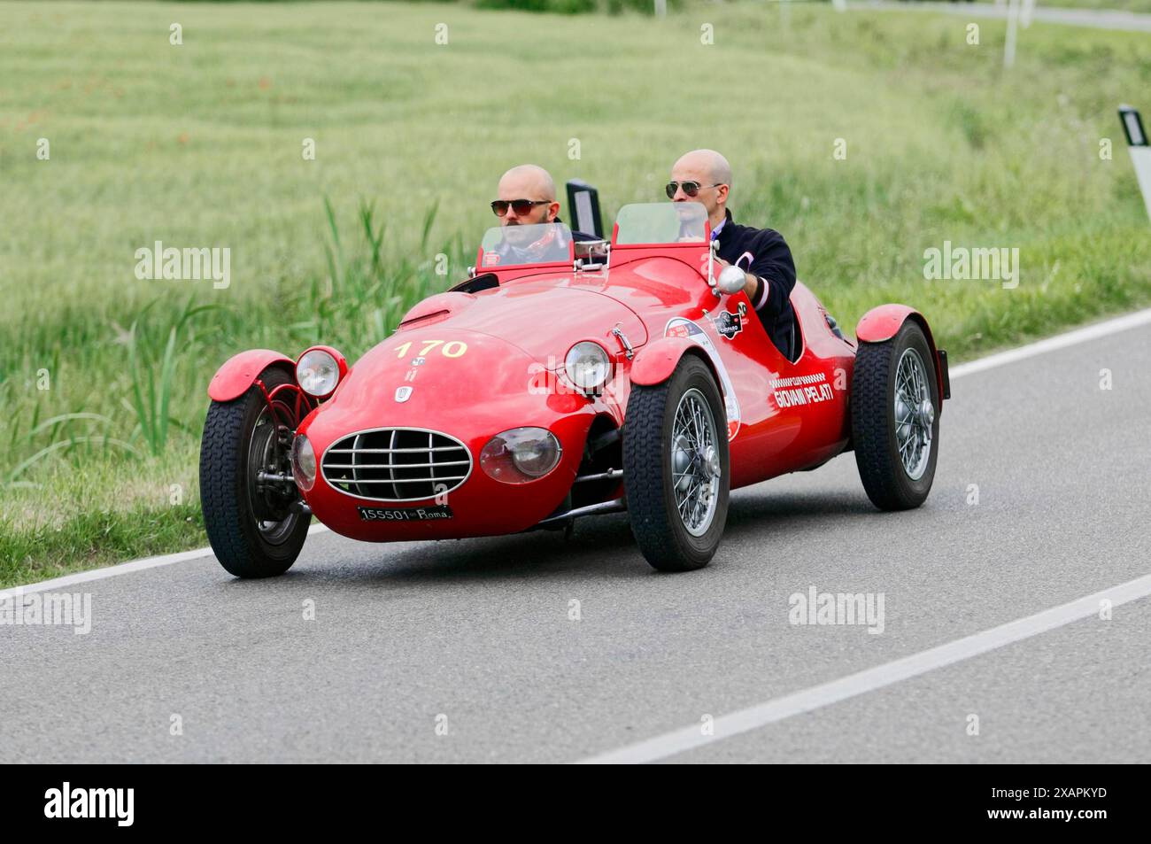 Red classic car with two drivers wearing sunglasses, driving on a quiet ...