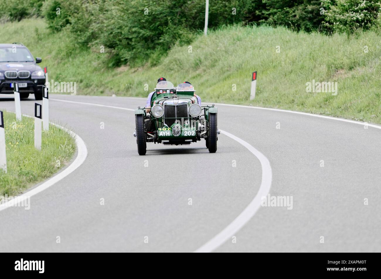 Historic green racing car driving along a winding country road ...