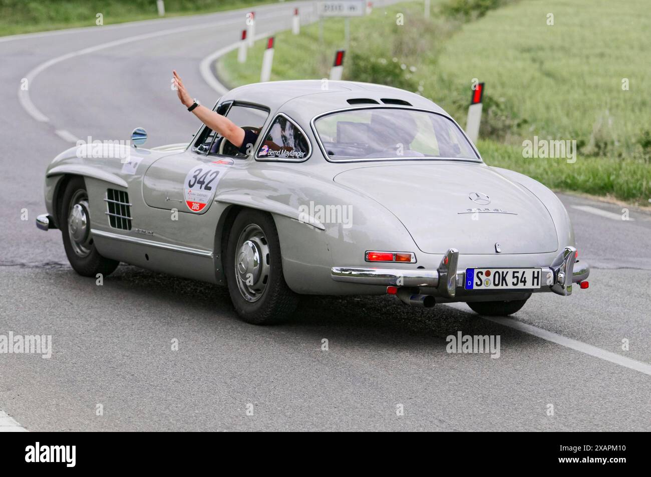 Silver classic car on a country road with driver giving a hand signal ...