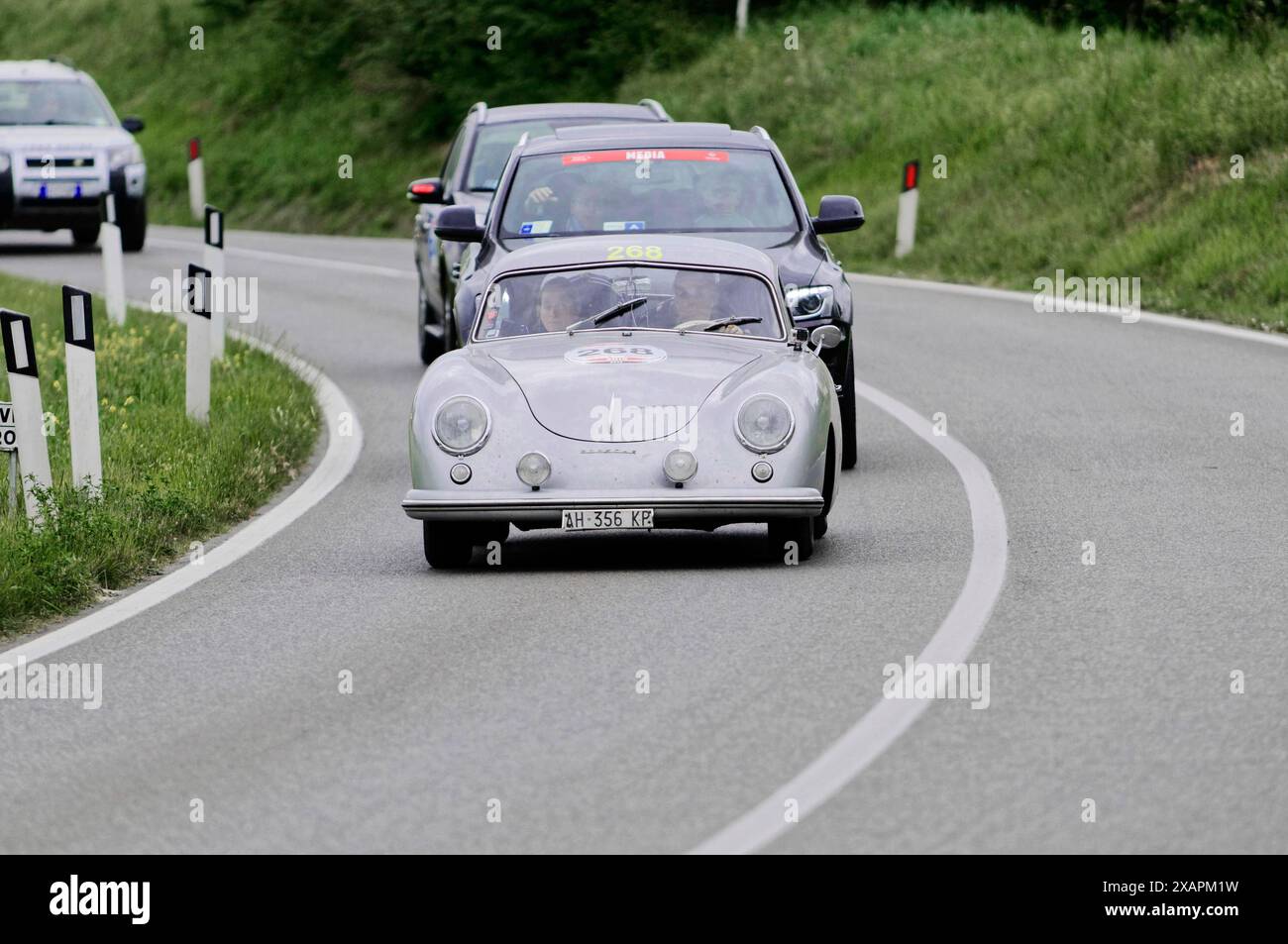 A grey classic racing car followed by other cars on a winding road ...