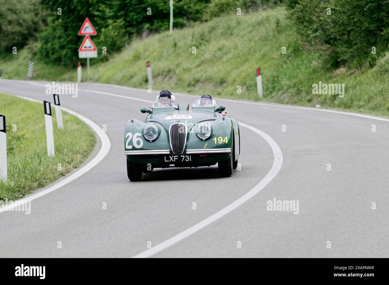 Two drivers in a green classic car drive on a winding country road ...