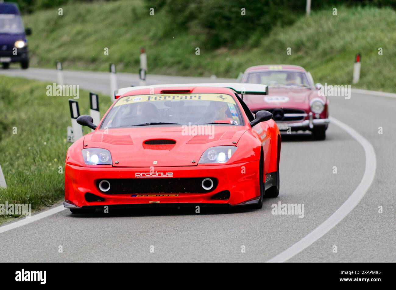 A red Ferrari sports car drives on a winding country road during a race ...