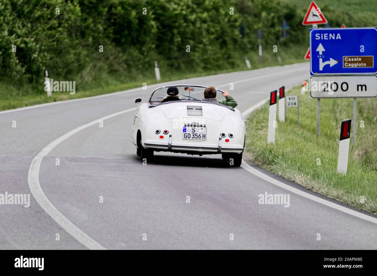 A white classic convertible is driving on a winding country road during ...
