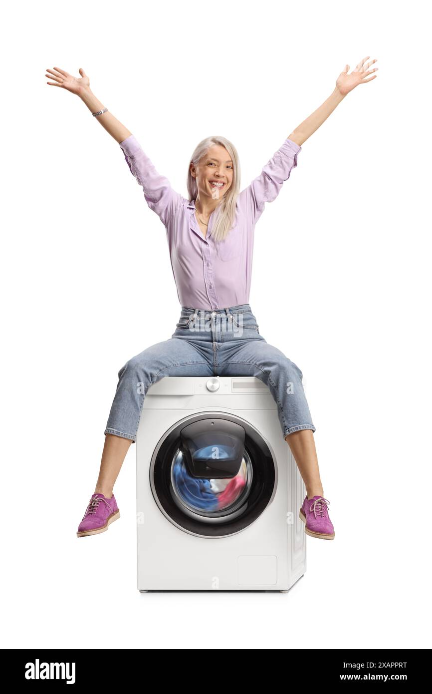 Smiling woman sitting on top of a washing machine and gesturing ...