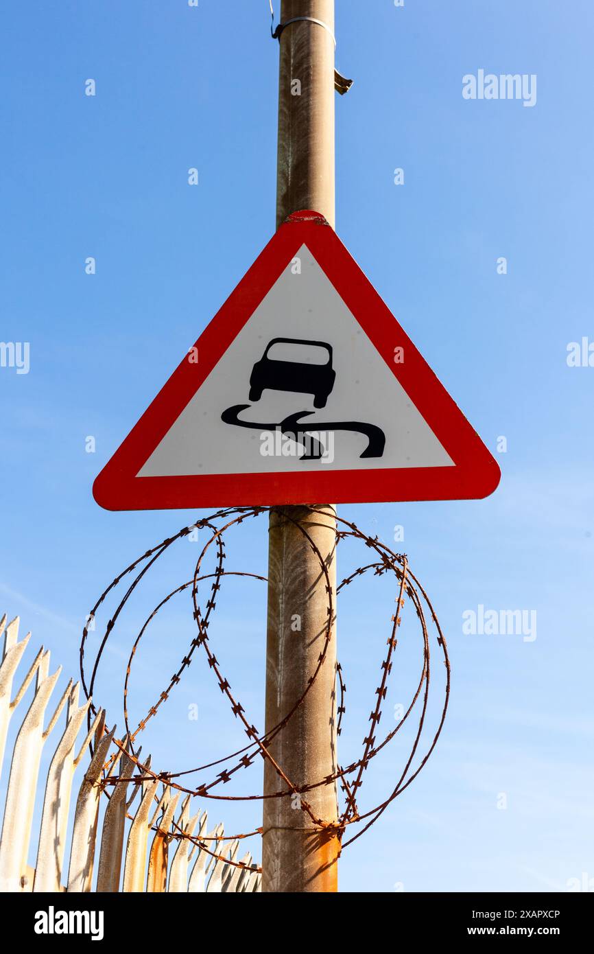 Slippery road sign on a rusty pole over some barbed wire and next to a ...