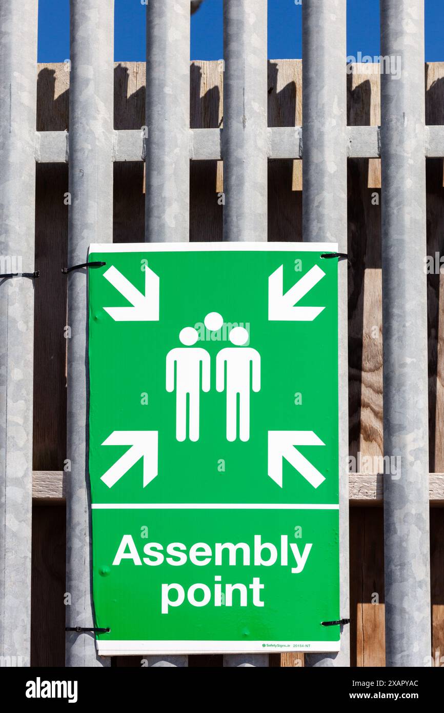 Green assembly point sign on a metal fence with a wood plank in the ...