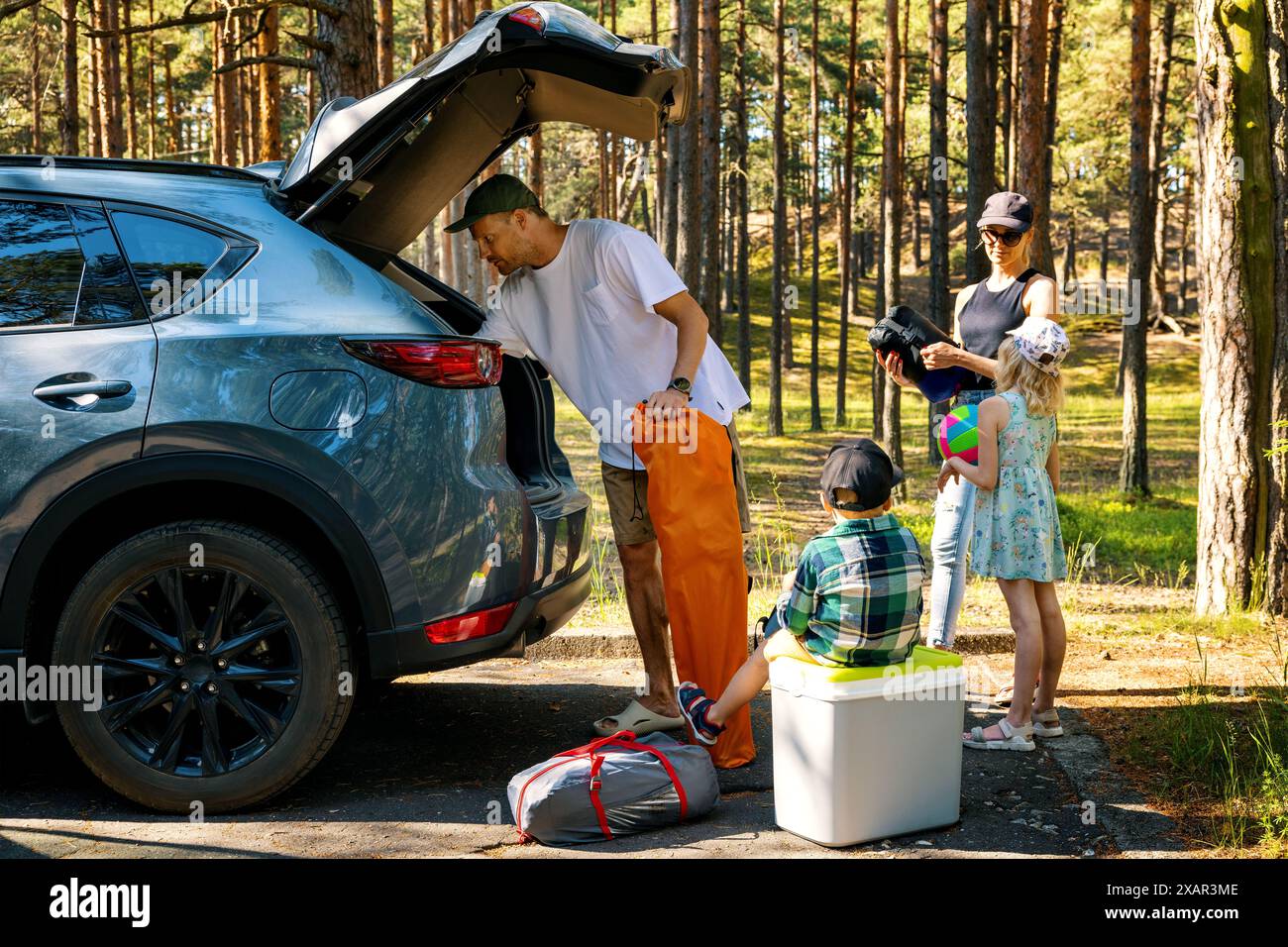 family with kids remove the camping supplies from car trunk at forest ...