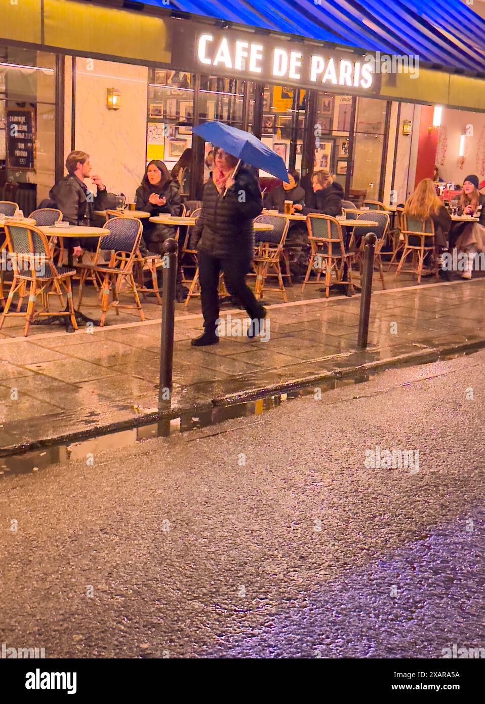 A woman carrying an umbrella walking past a Parisian cafe on a rainy ...