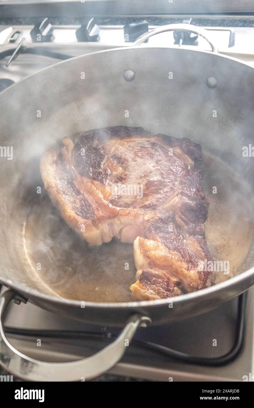 A thick cut of aged beef steak is sizzling in a pan with beef fat ...