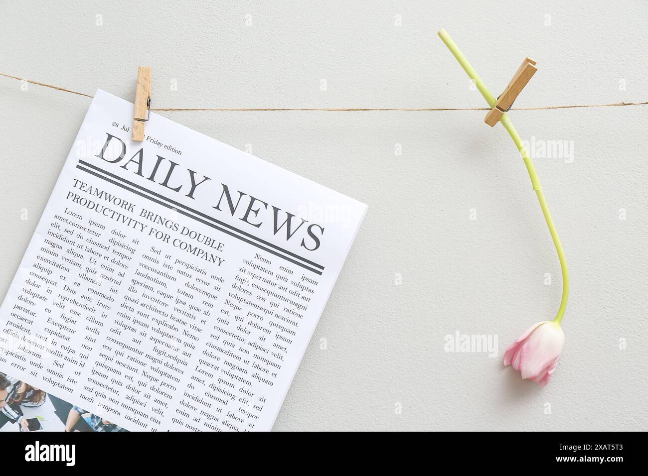 Newspaper and tulip flower hanging on rope against white background ...