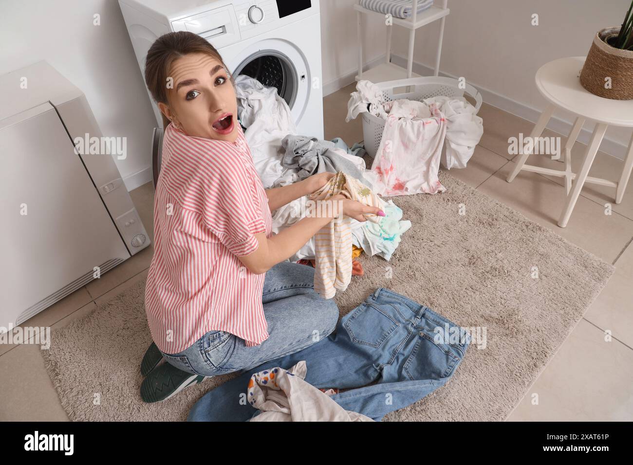 Shocked young woman with dirty laundry near washing machine at home ...
