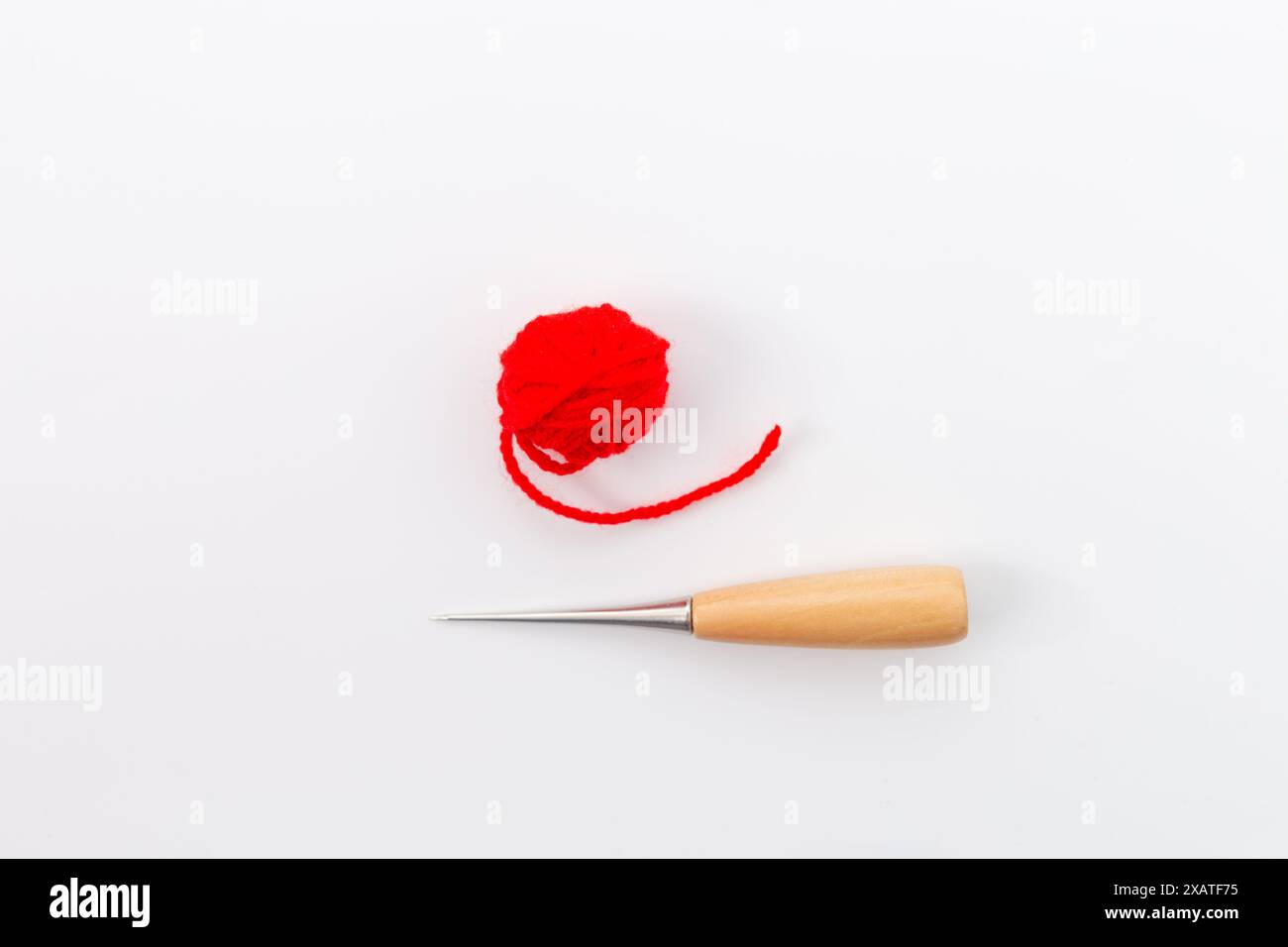 Red yarn ball and unraveled strand beside wooden-handled steel awl on ...