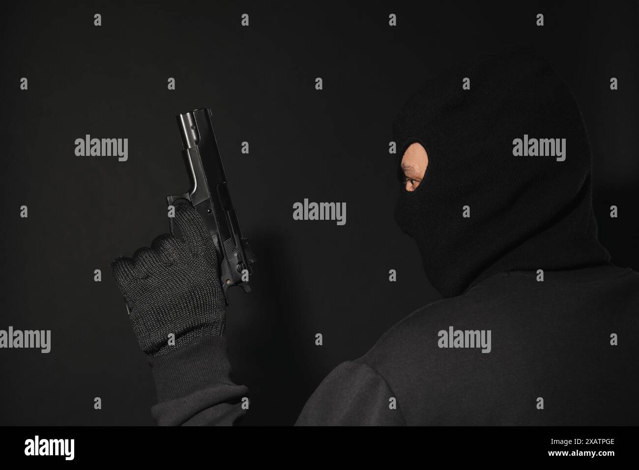 Dangerous masked criminal with gun on black background. Armed robbery ...