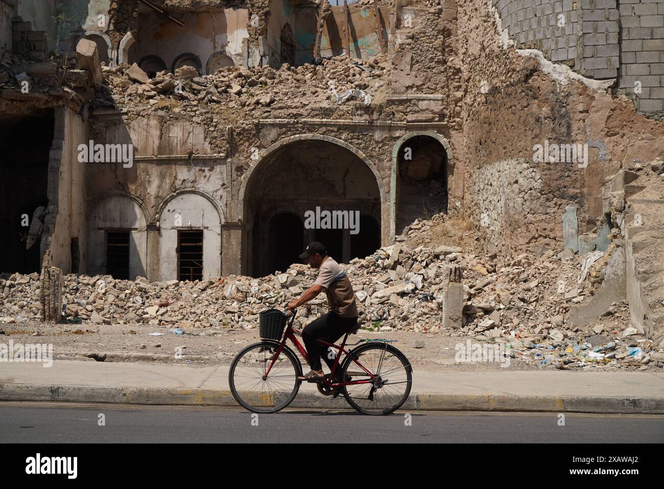 Mosul, Iraq. 08th June, 2024. A man rides his bicycle next to destroyed ...