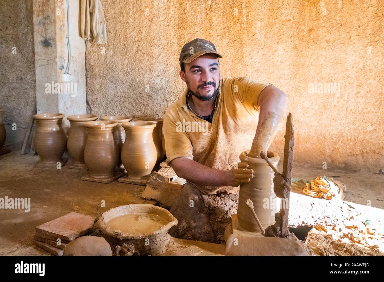 A man works on a pottery piece in a room with many other pieces. The ...