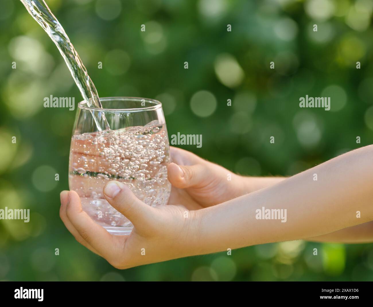 child hands holding glass and water pouring with green garden on the ...