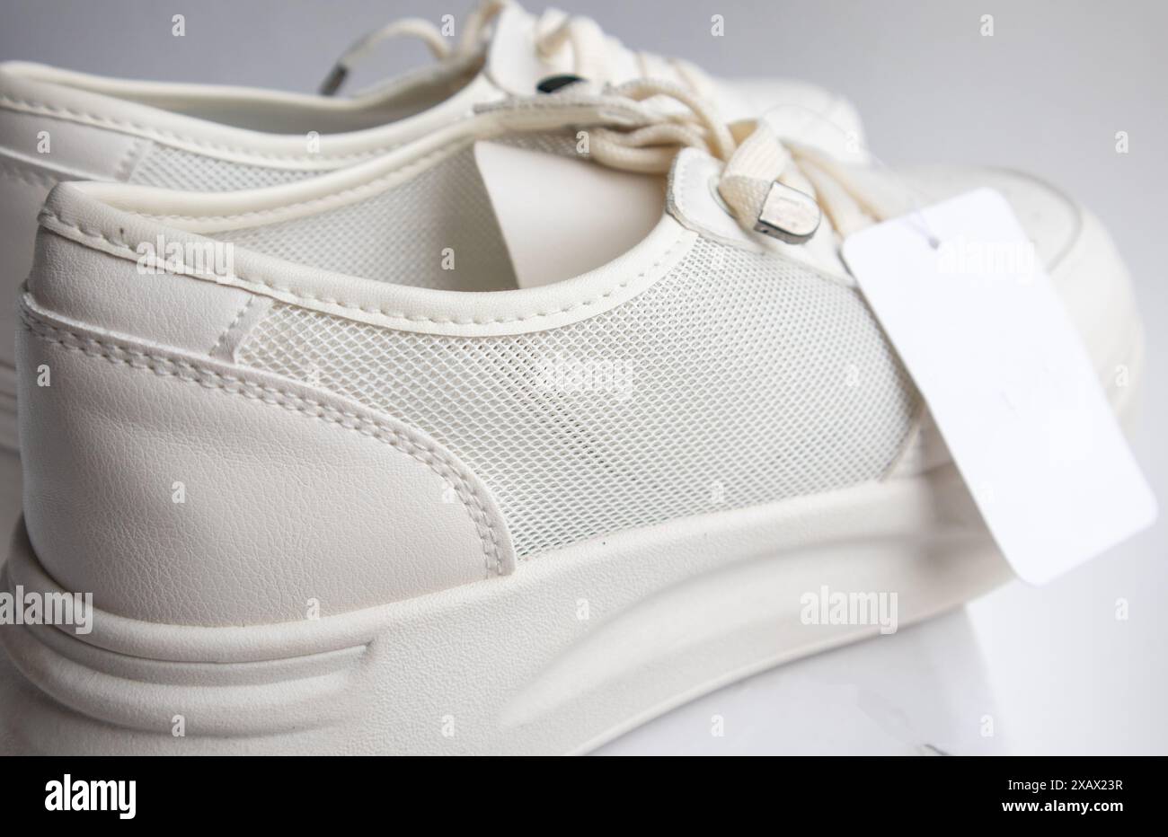 A close-up of a stylish pair of white women's sneakers with a label ...