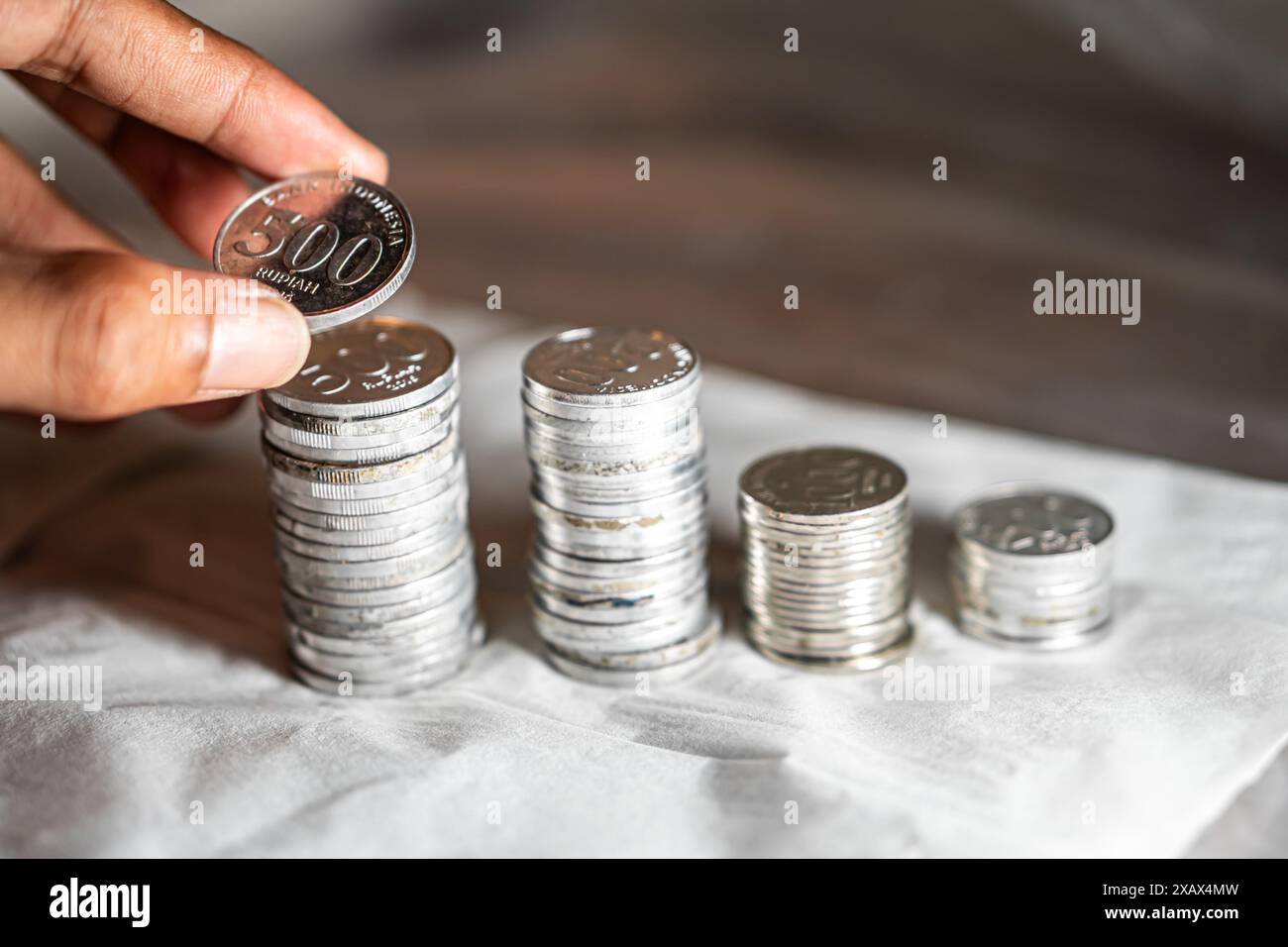 A person stacking silver coins in ascending order on a white surface ...