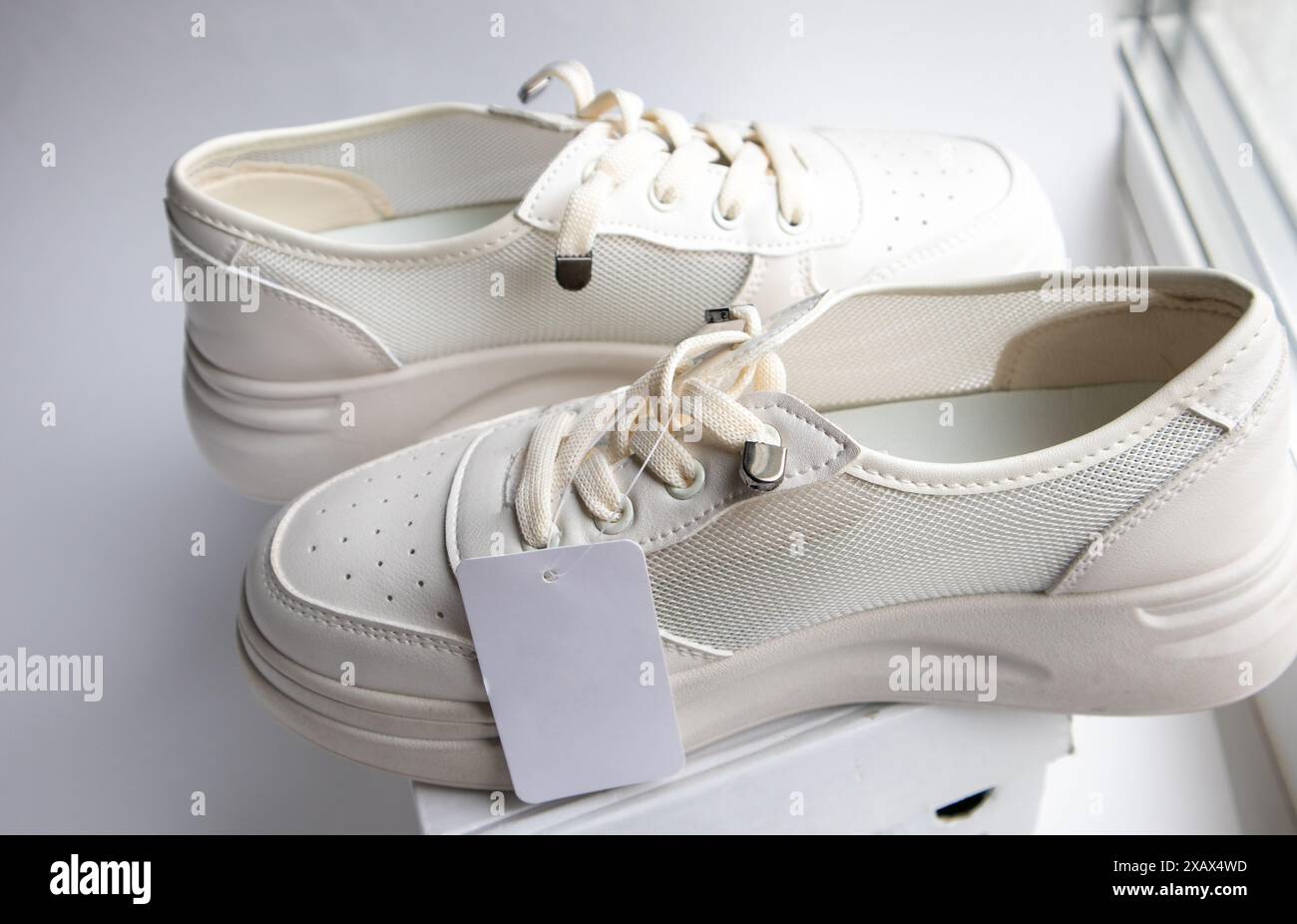 A close-up of a stylish pair of white women's sneakers with a label ...