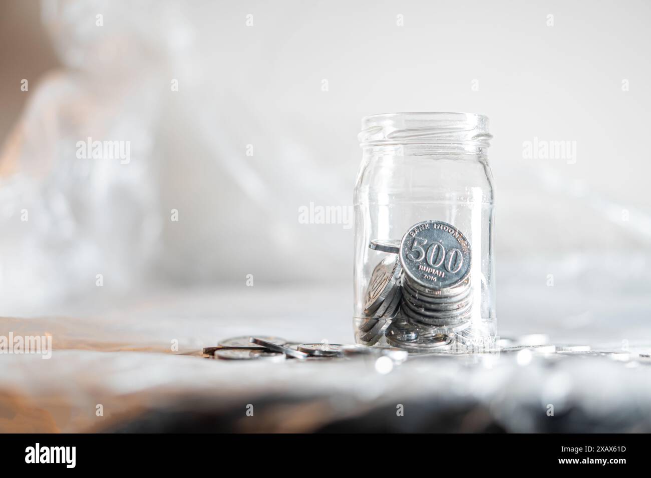 A glass jar filled with 500 Korean won coins, placed on a reflective ...