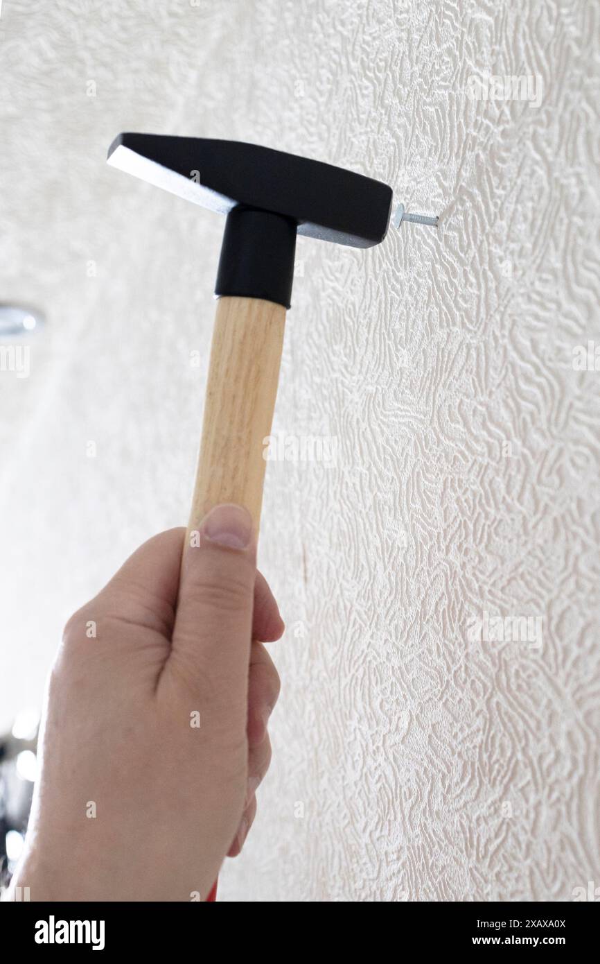 male hand with hammer drives nail into white wall iat home Stock Photo ...
