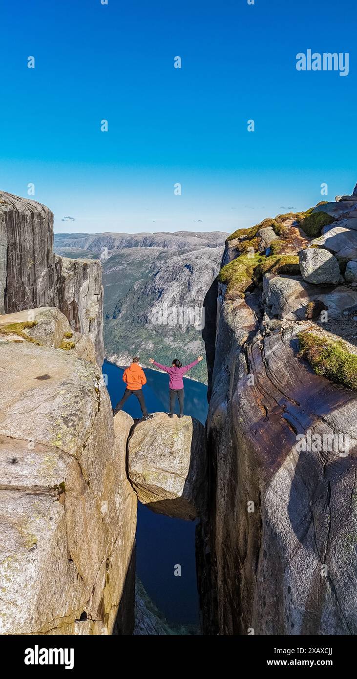 Two people stand on the edge of Kjeragbolten, a famous cliff in Norway ...