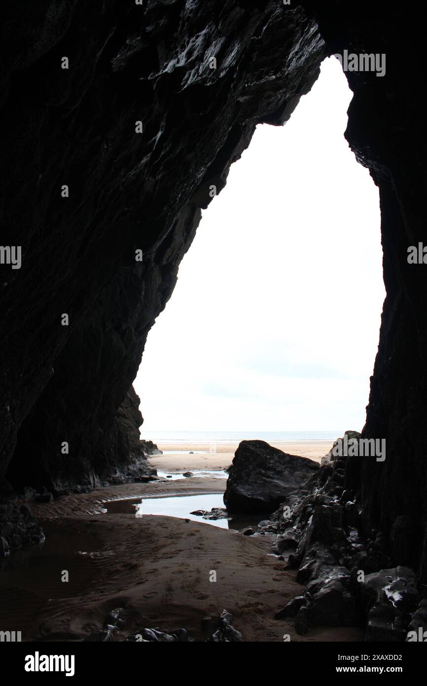 A photograph of a beach scene looking out of a cave at Three Cliffs Bay ...