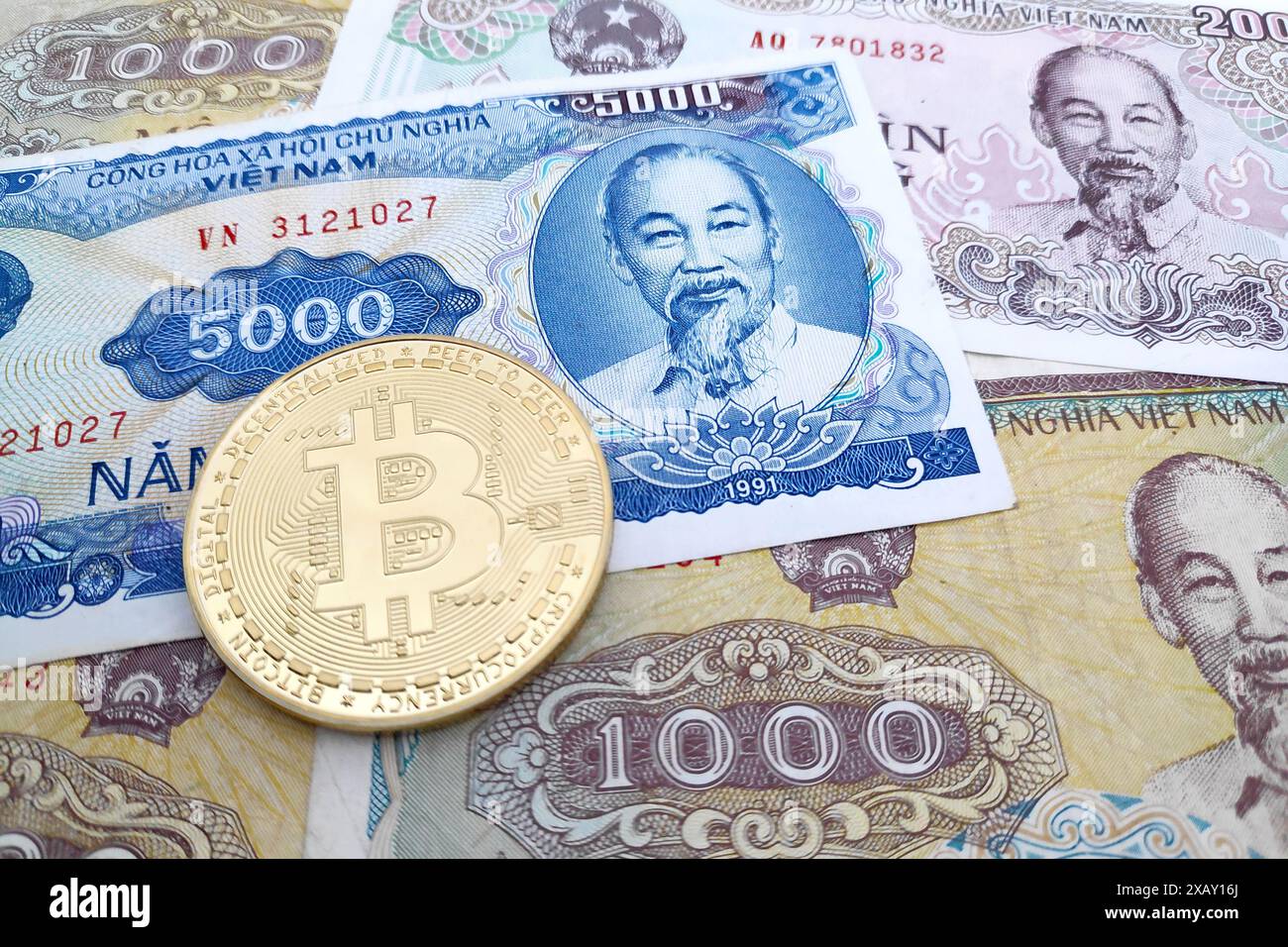 Close-up on a golden Bitcoin coin on top of a stack of Vietnamese Dong ...