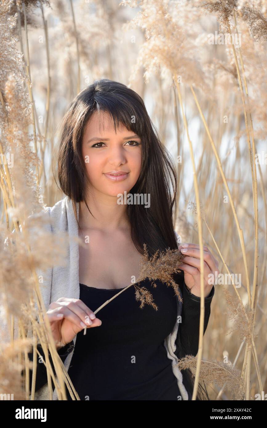 Brunette woman in tall dry grass, looking forward in natural daylight ...