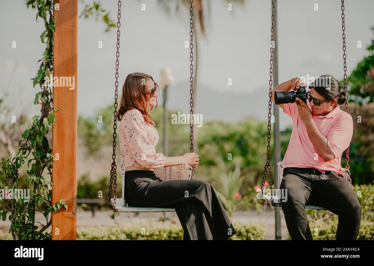 Boyfriend taking a photo of his girlfriend on a swing in a park ...