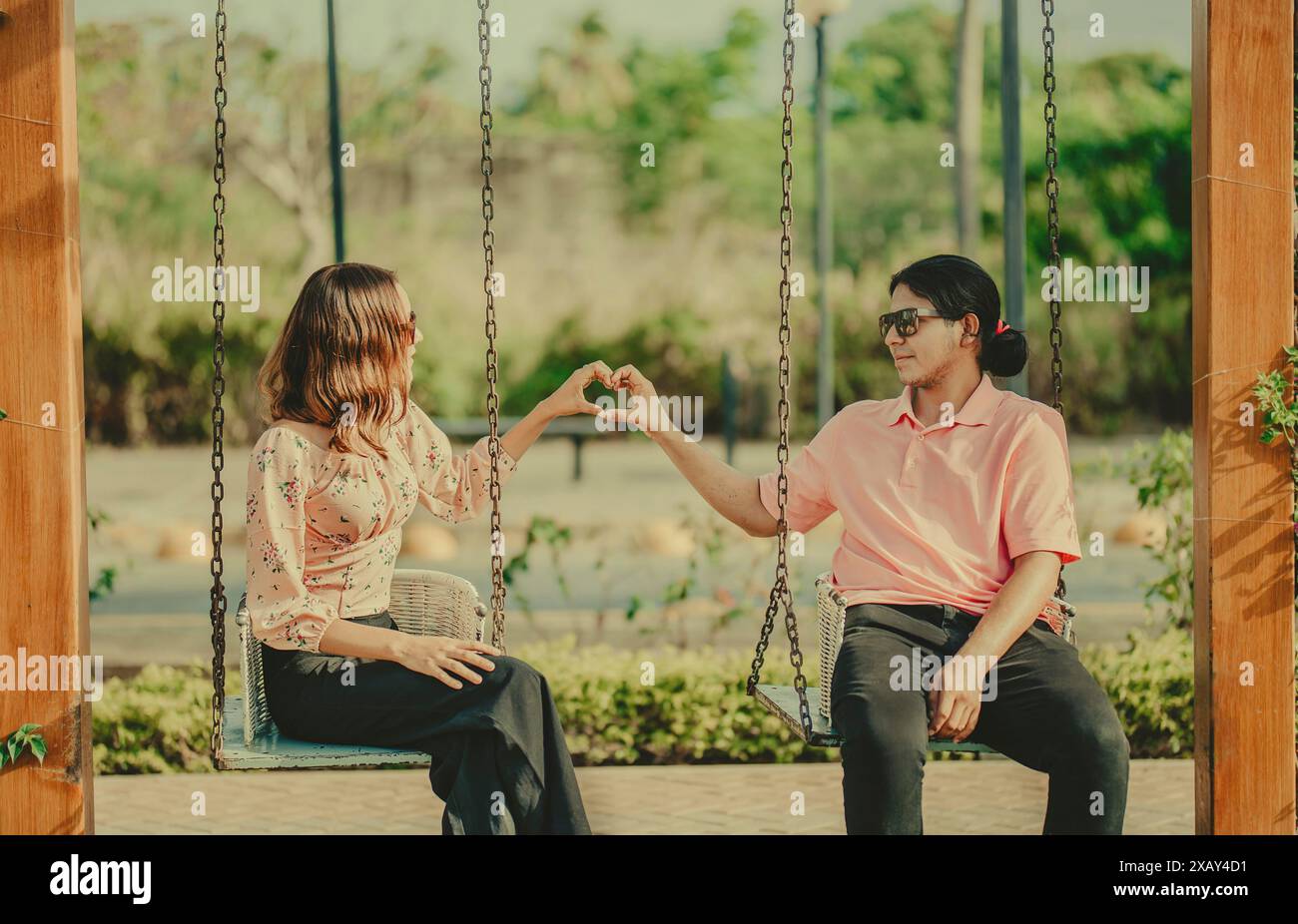 Young couple in love sitting on a swing making a heart shape. Happy ...
