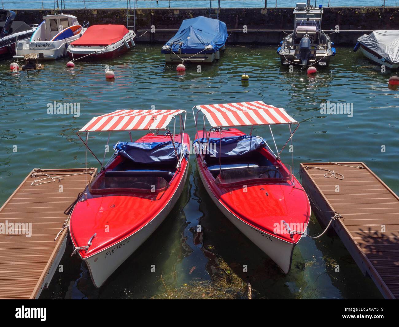 Two red boats with striped canopies lying side by side on a jetty in a ...