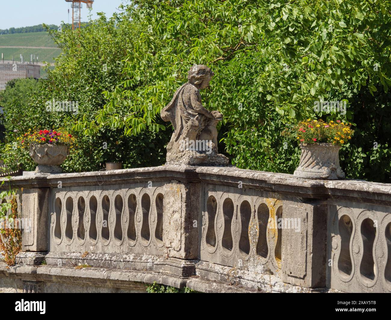 Stone statue on an old balcony railing, surrounded by green trees and ...