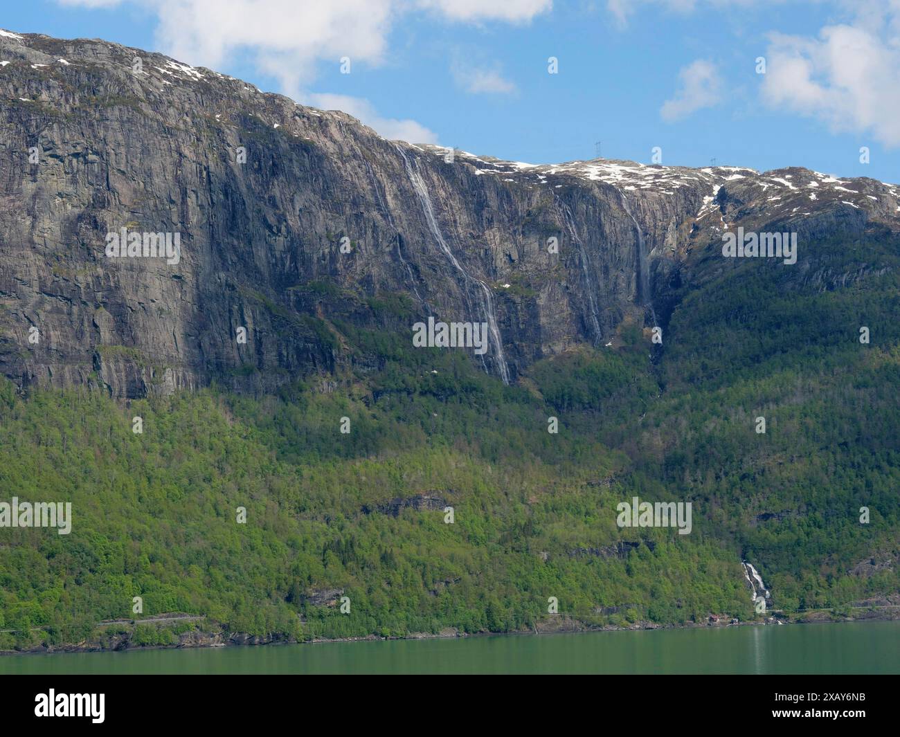 High cliffs with waterfalls and snow-capped mountains under a clear ...