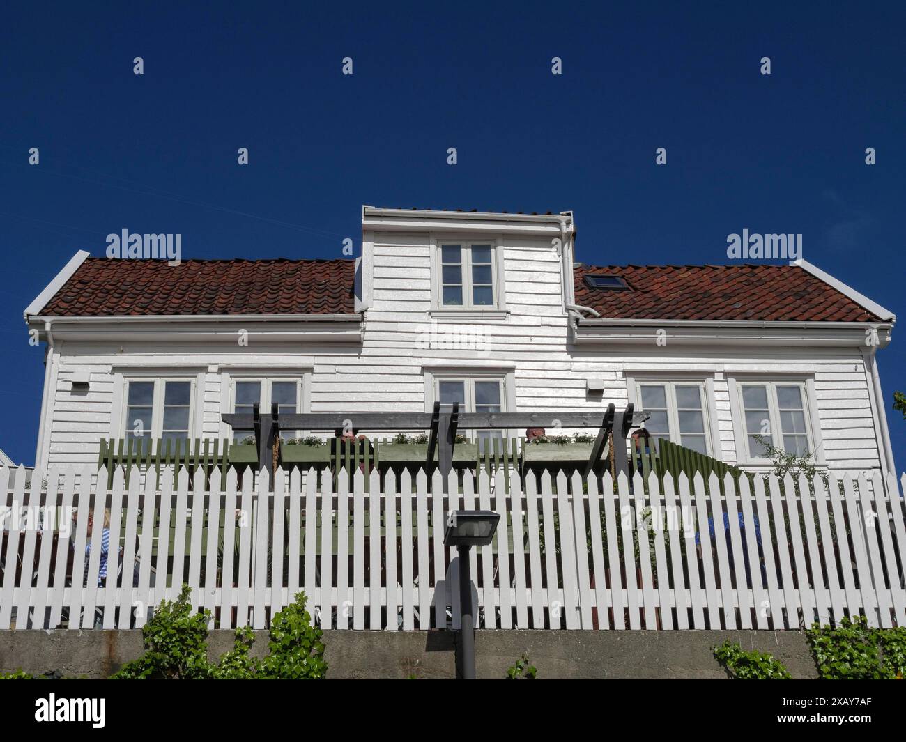 White house with red roof and balcony behind a white wooden fence under ...