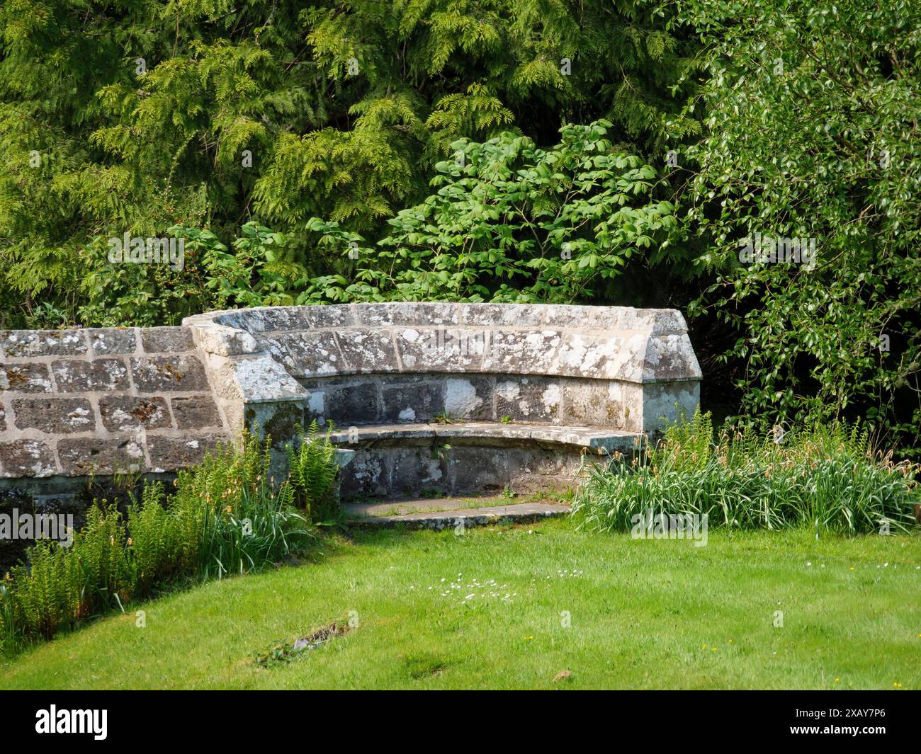 An old stone bench in a historic garden surrounded by green trees and ...