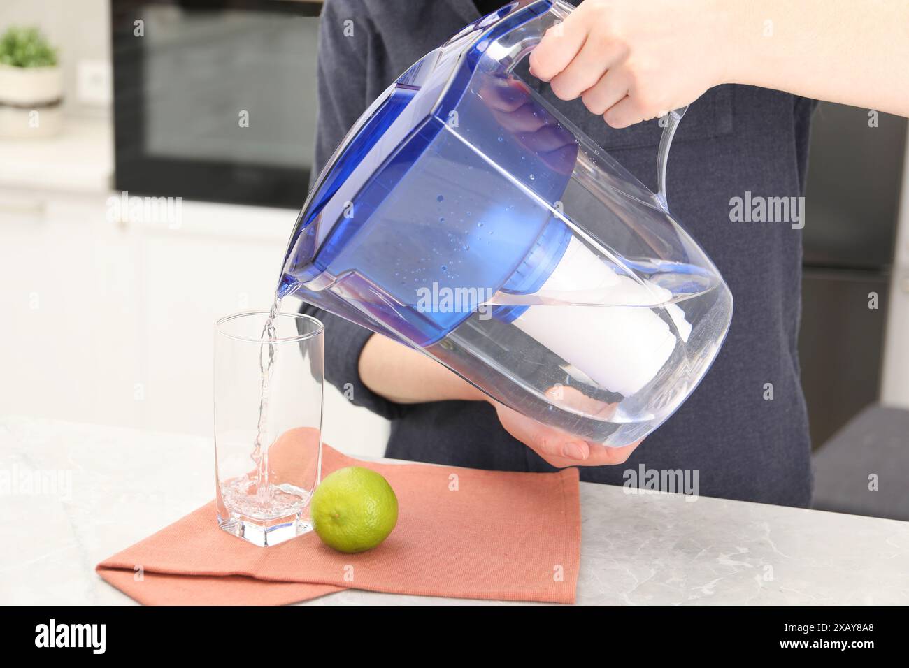Woman pouring water from filter jug into glass at light marble table in ...