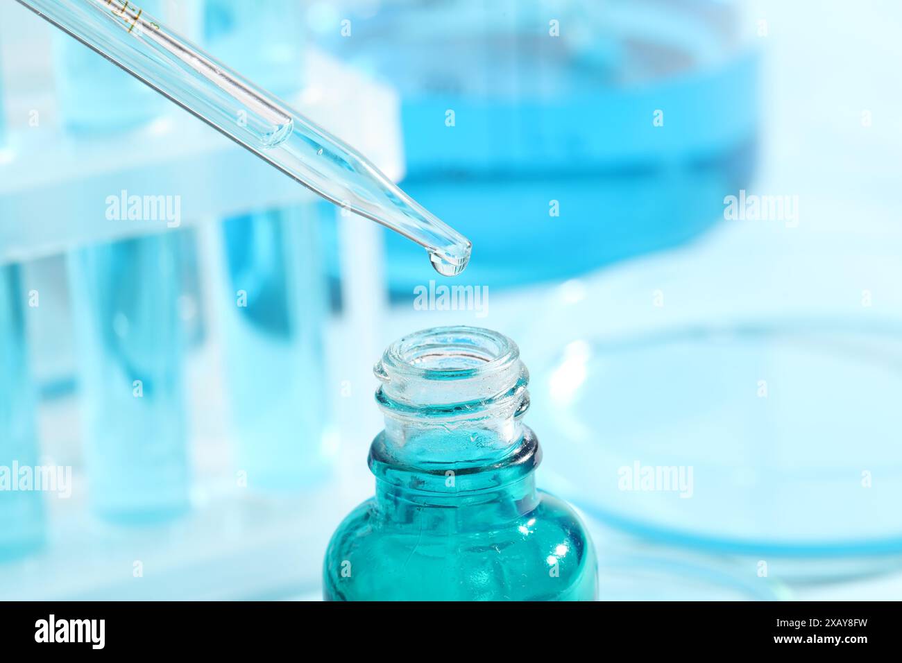 Dripping liquid from pipette into bottle on blurred background, closeup ...