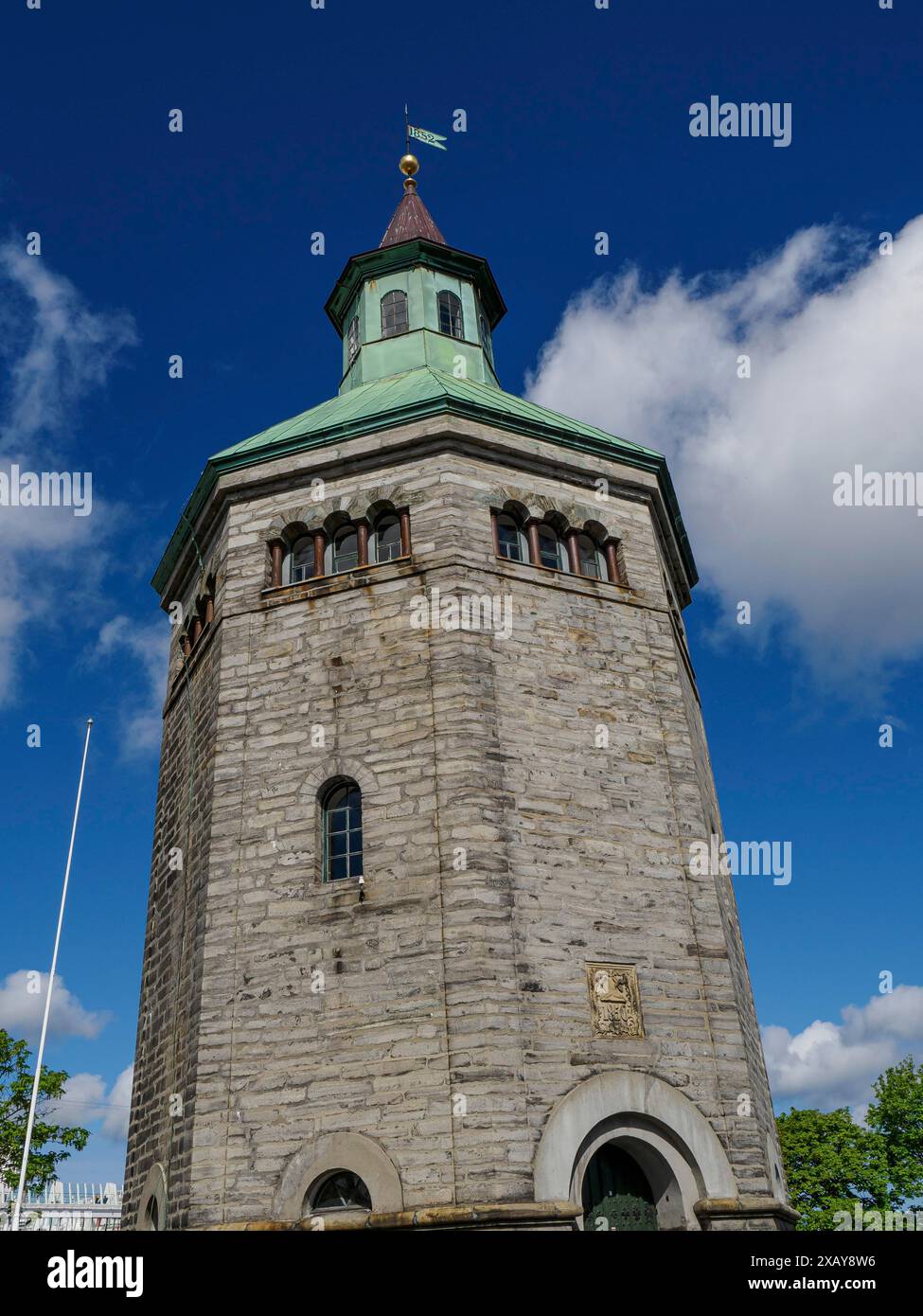 An old stone tower with a green roof rises into the sunny blue sky ...