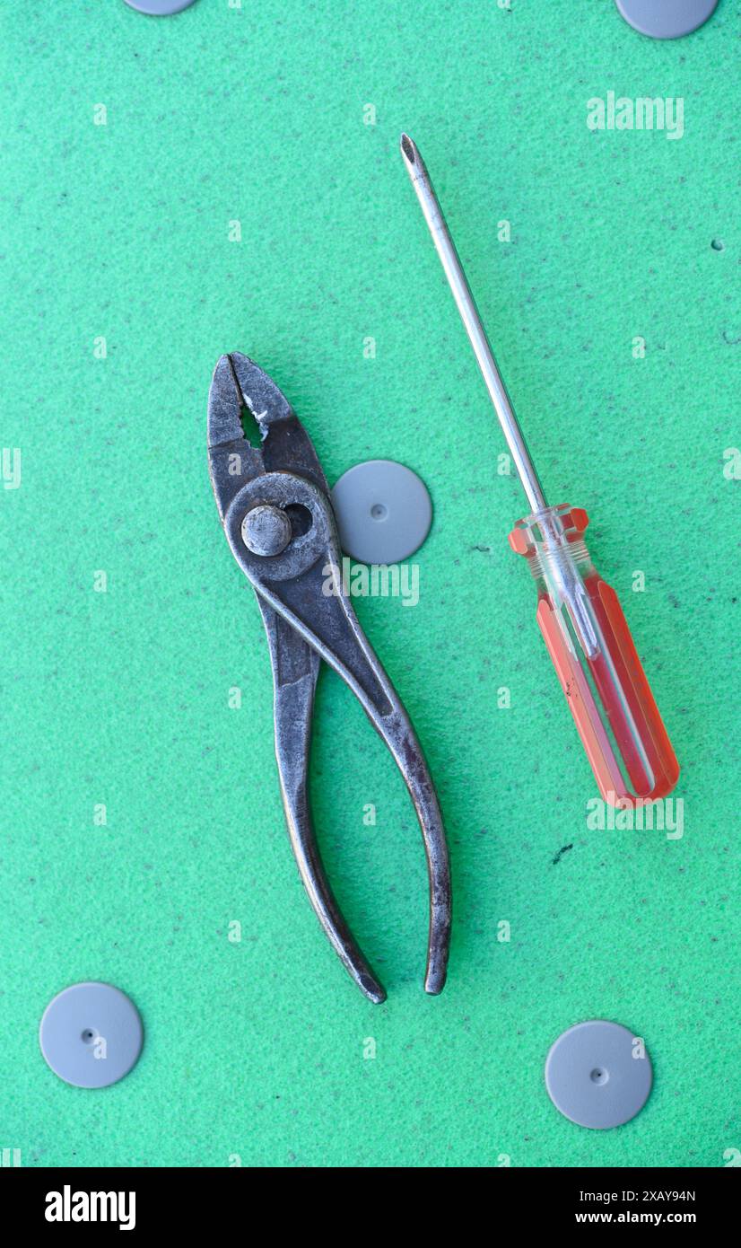 Pliers and a screwdriver on a green background. Tools Stock Photo - Alamy