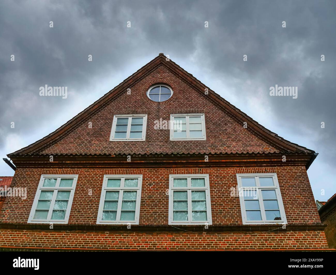 A brick house with large windows and a pointed roof under a gloomy sky ...