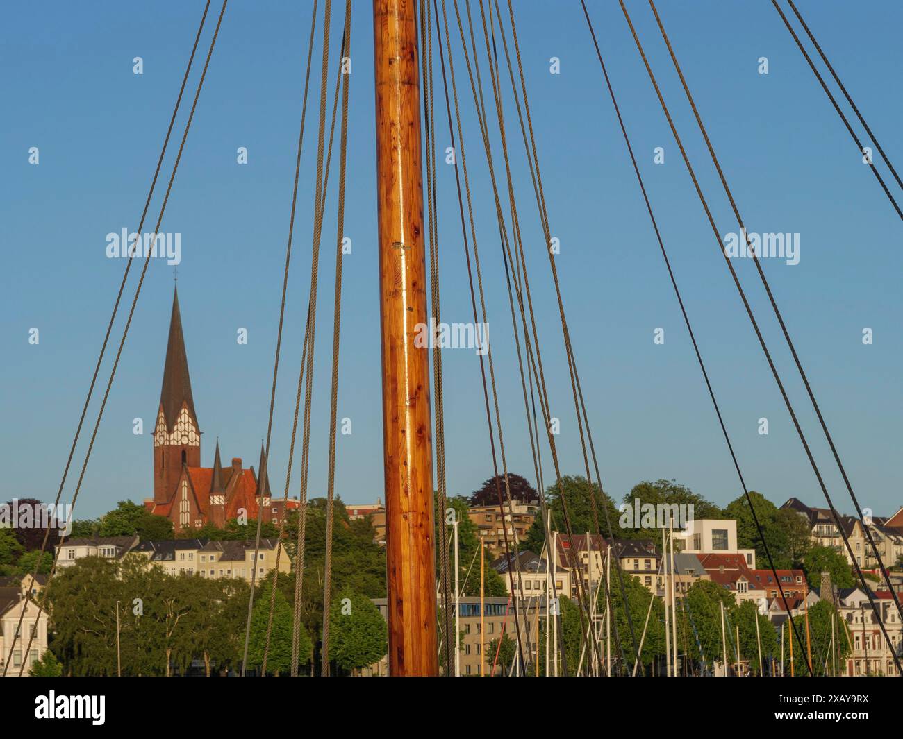 A tall sailing mast in the foreground with a church tower and sailing ...