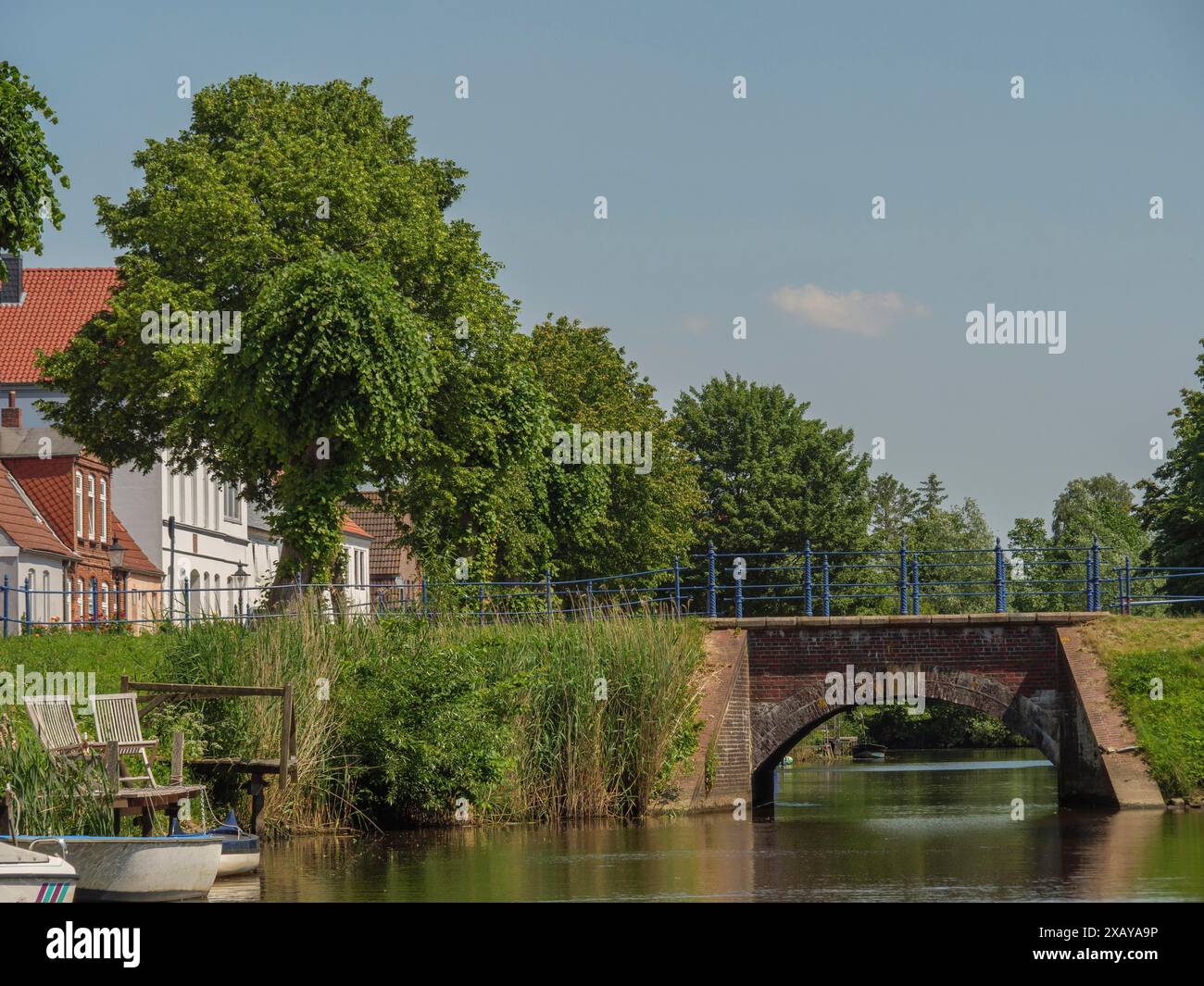 Small riverbank with a bridge, surrounded by green trees and boats in ...