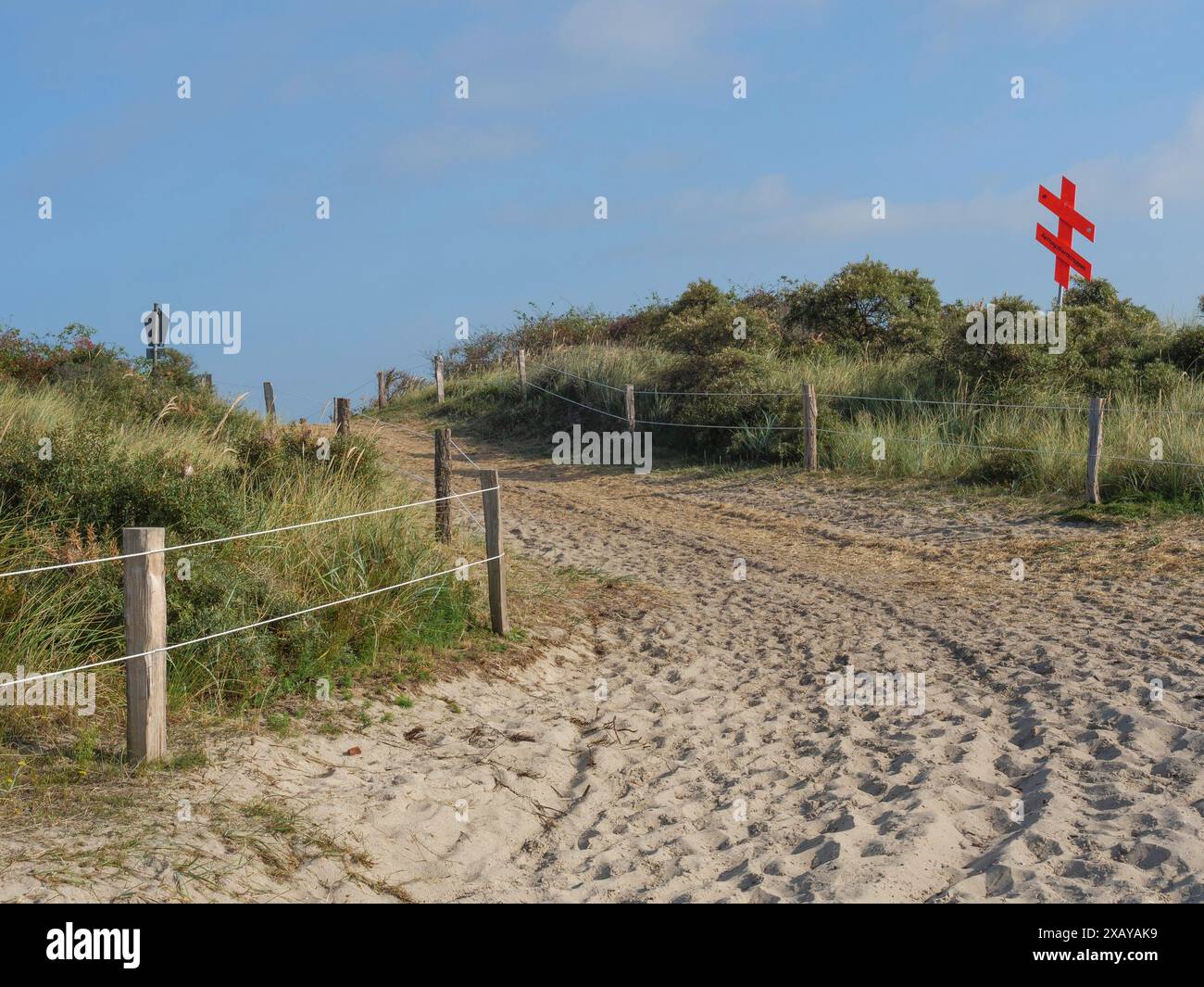 Sandy path leads through dunes and vegetation, a red cross sign is ...