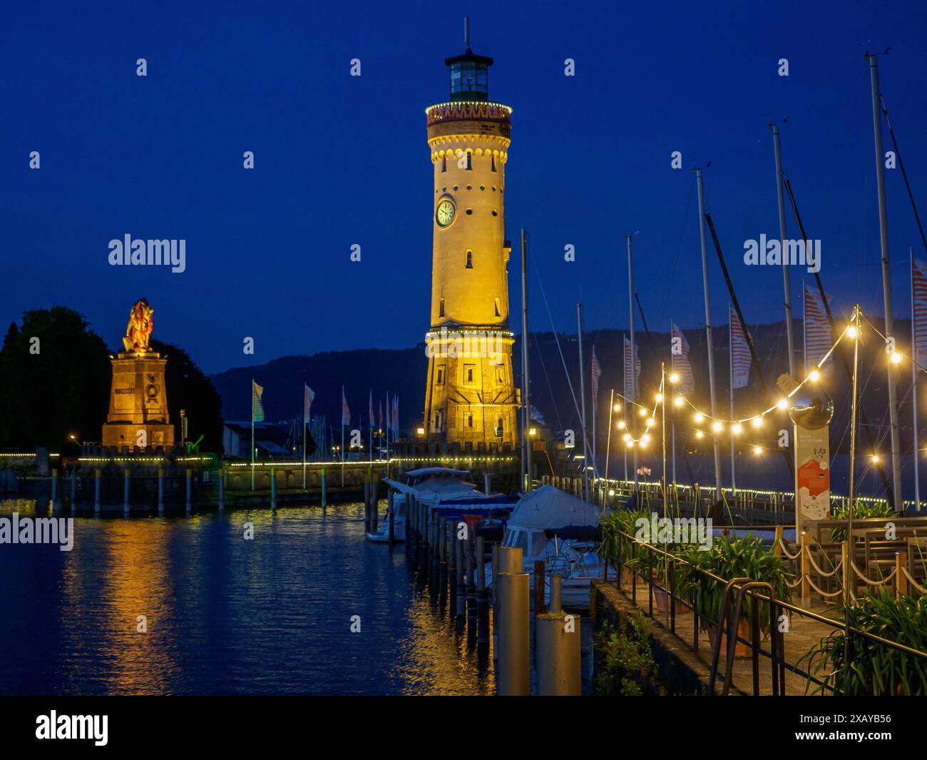 An illuminated lighthouse at night, surrounded by boats and lights in ...