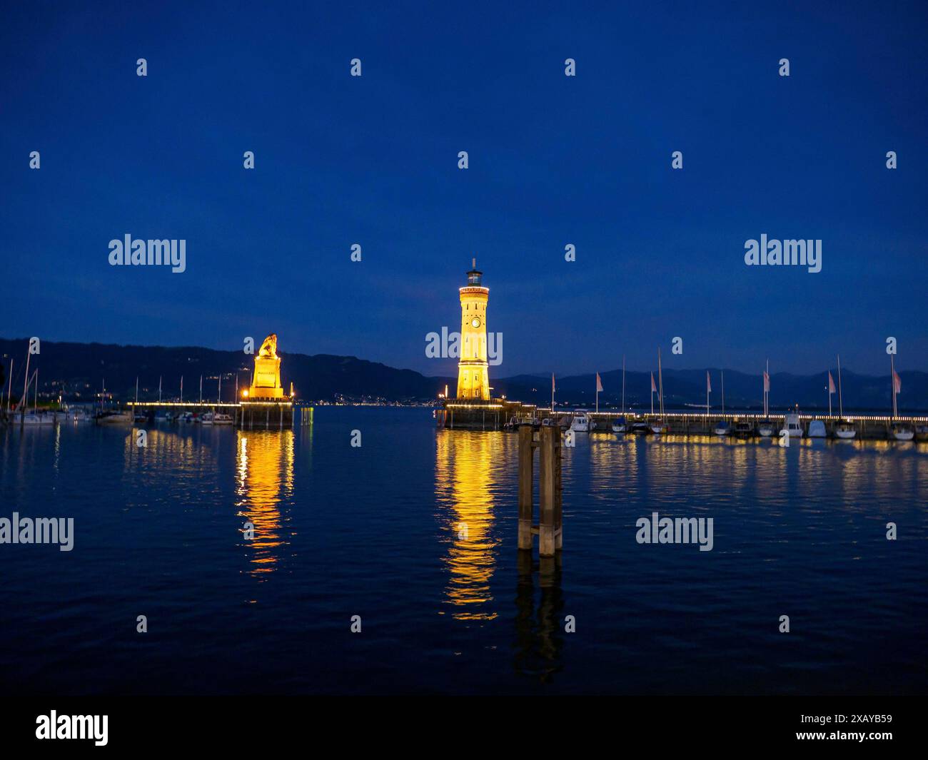 Night scene of a harbour with illuminated lighthouse and lion sculpture ...