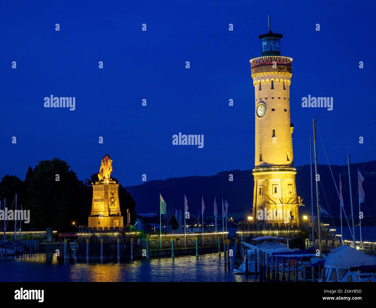 A lighthouse and a statue at night, brightly lit and reflected in the ...