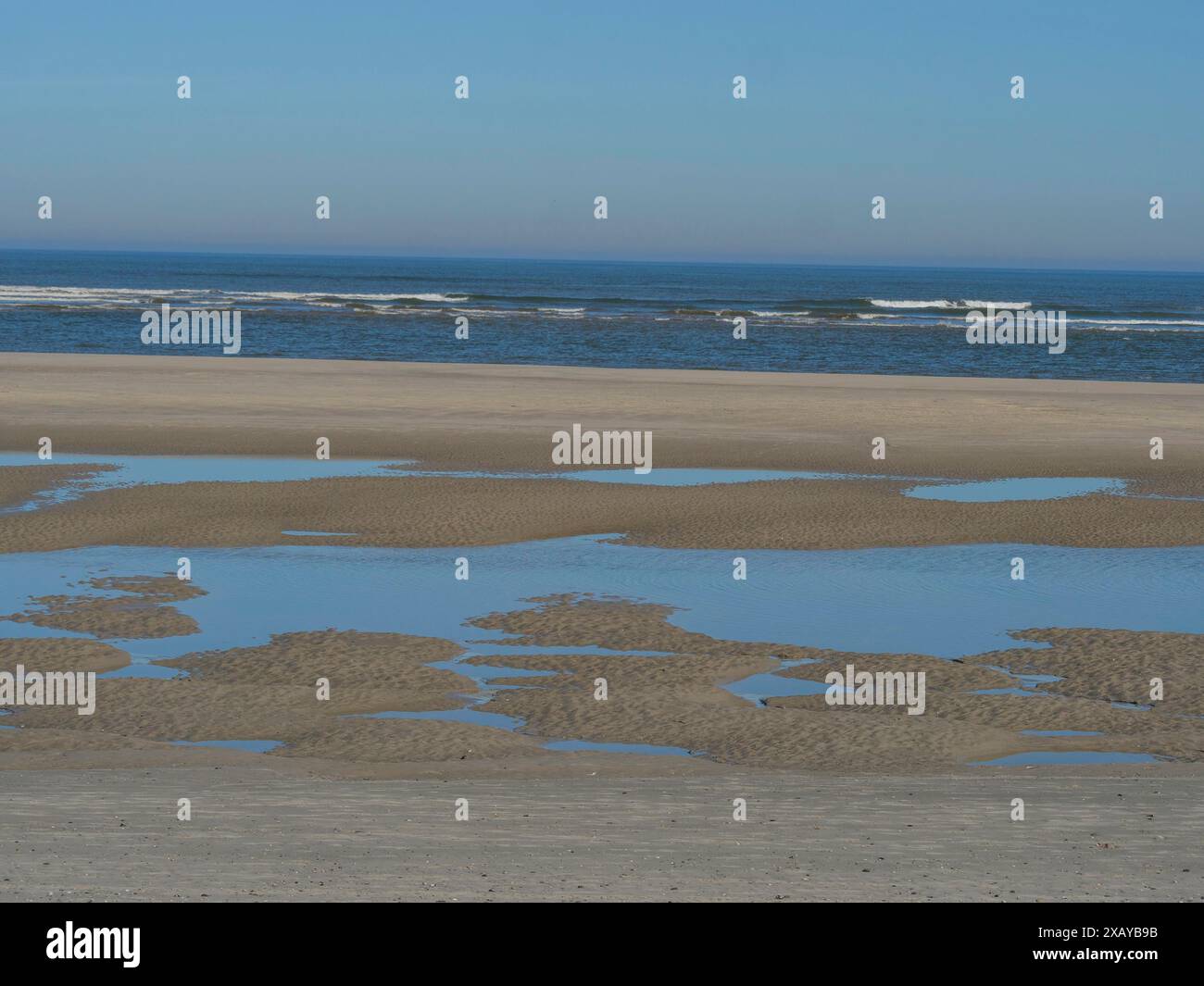 Quiet sandy beach with puddles of water and a view of the wide, calm sea, langeoog, germany ...