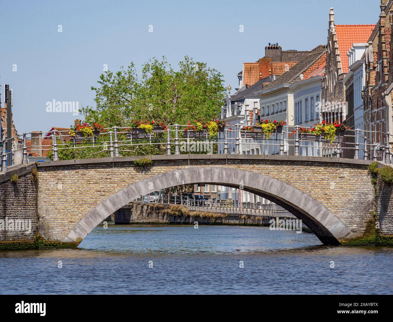 A stone bridge spans a canal, lined with flowers and historic buildings ...