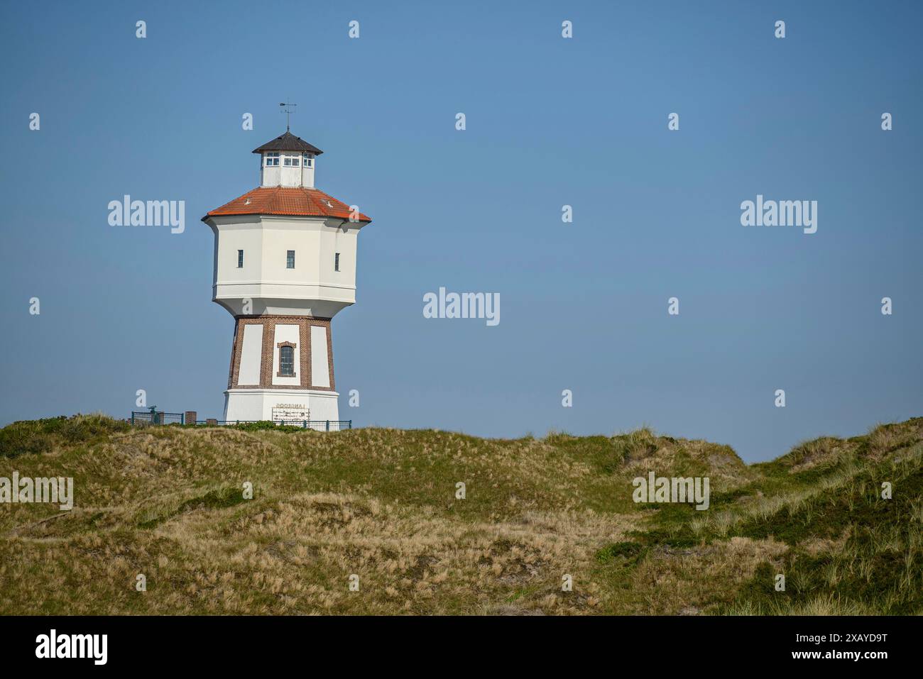 Lighthouse on grassy dunes under a blue sky in a peaceful landscape ...